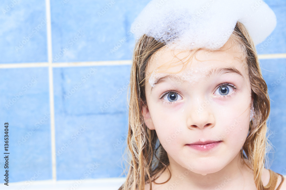 Adorable child blond girl with shampoo foam on hair taking bath ...