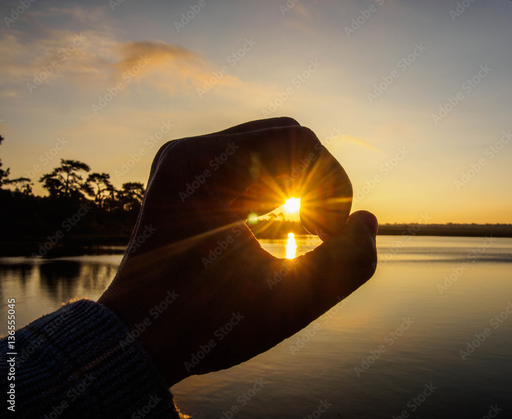 hand symbol against sunlight at sunrise near the pond on the mountain ...