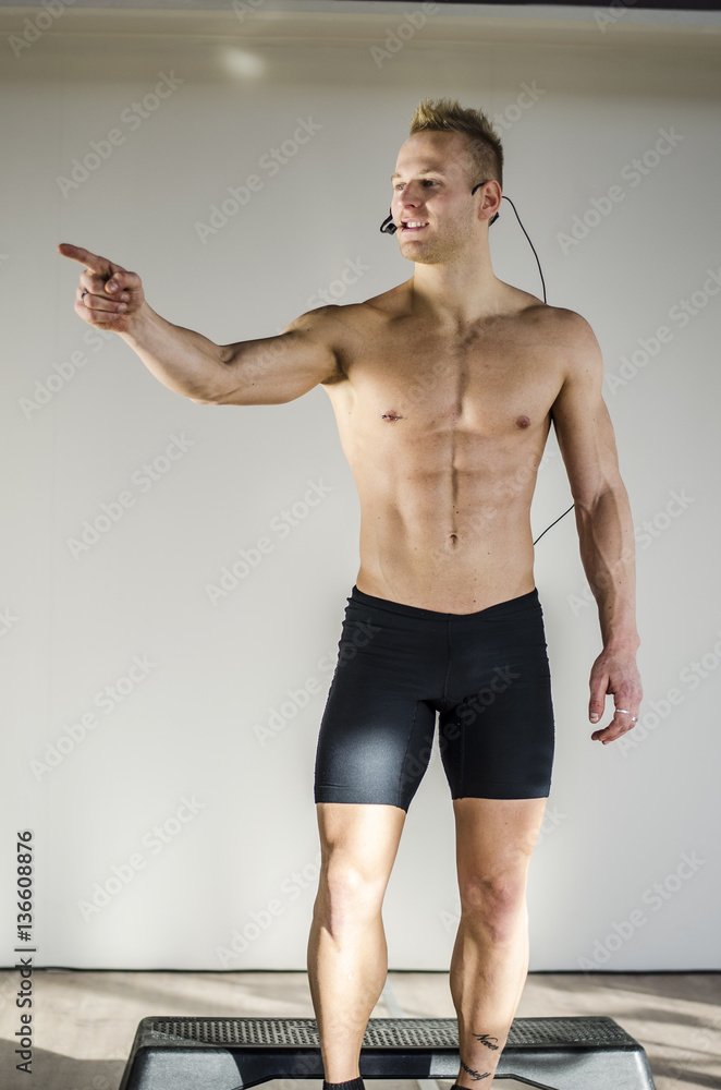 Young aerobics male coach shirtless leaning on step teaching class ...