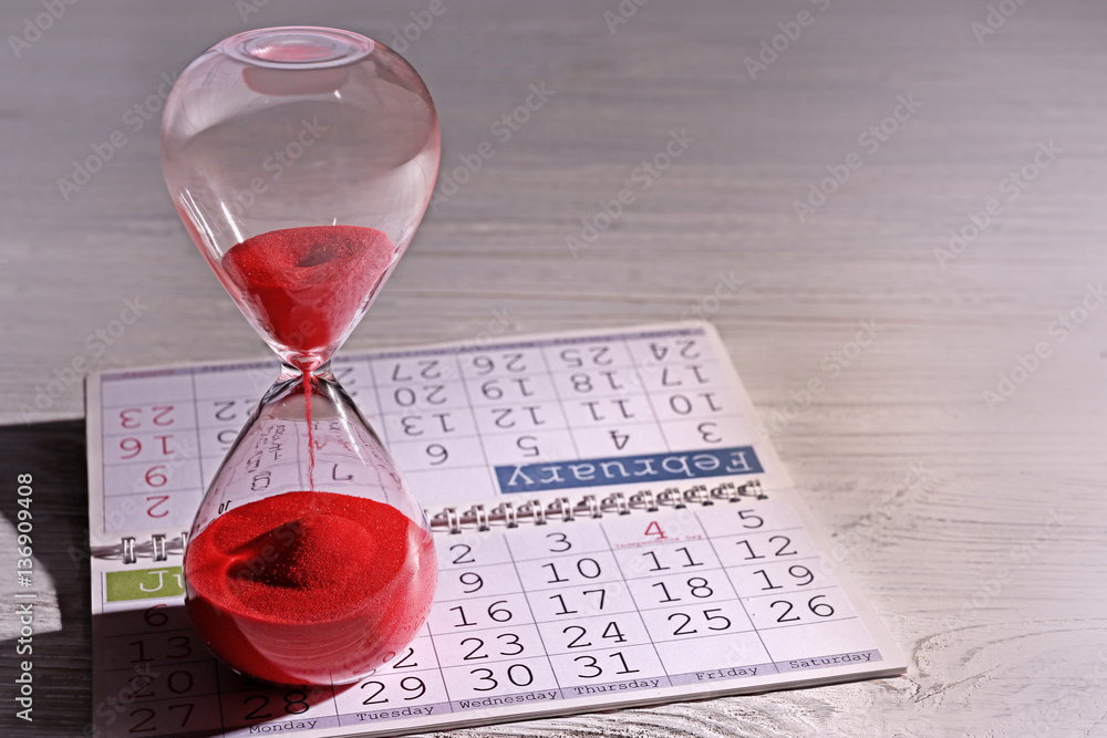 Time passing concept. Crystal hourglass with red sand and calendar on ...