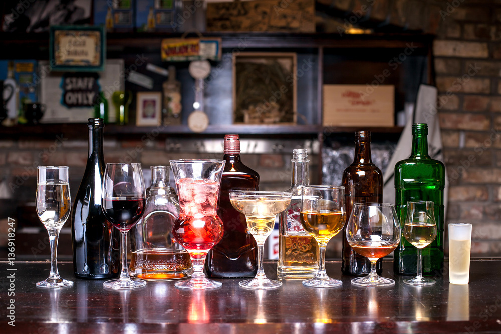 many different bottles of alcohol in different shapes, glasses with ...