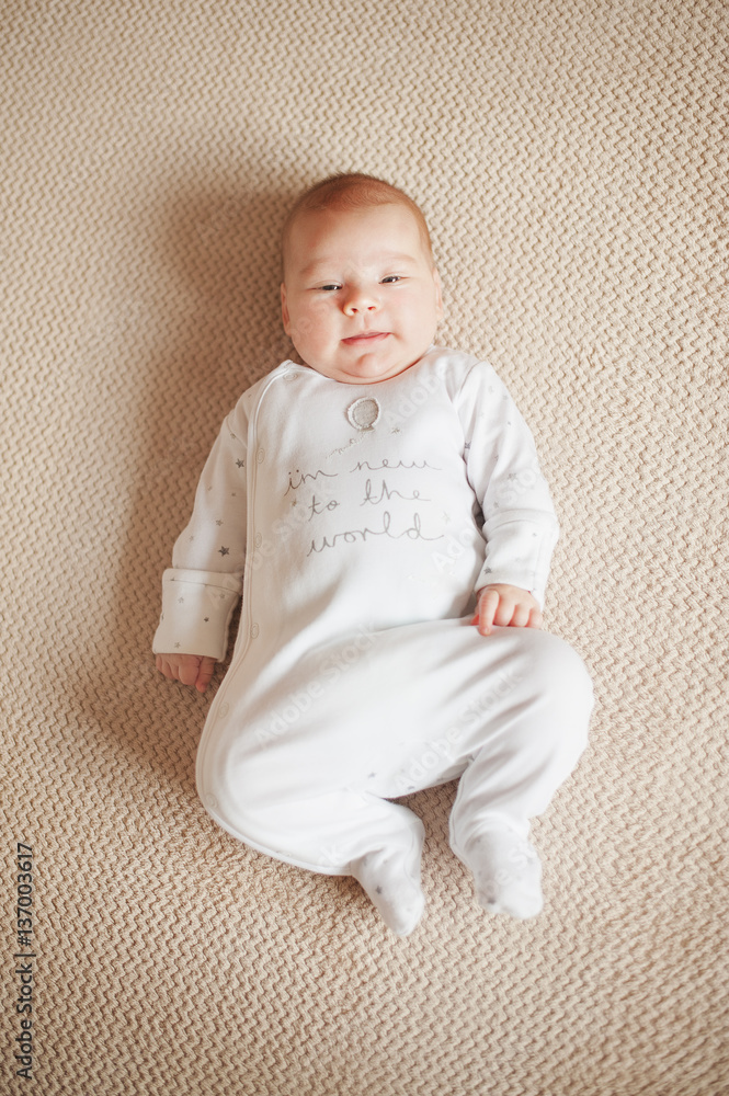 baby in white body suit lying on his back the sheet looking straight at ...