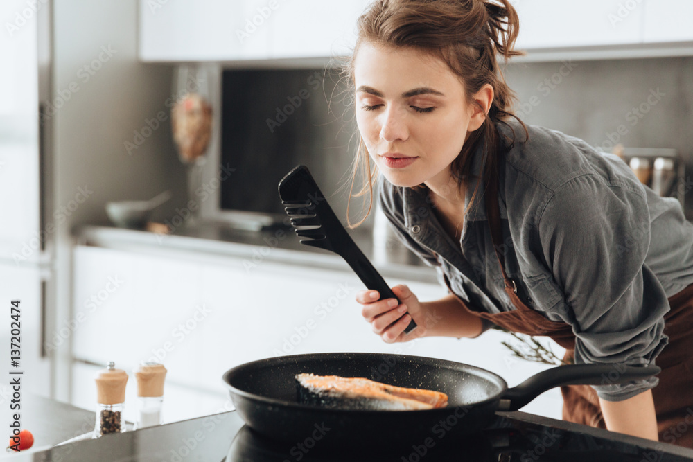 Beautiful lady standing in kitchen while cooking fish Stock Photo ...
