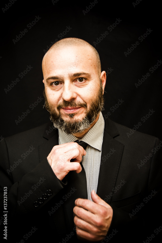 Handsome, bald man with beard, in suit and tie, on black background ...