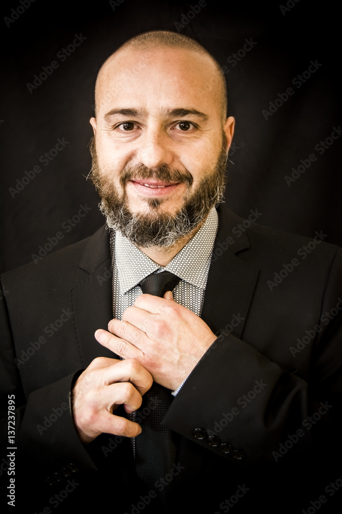 Handsome, bald man with beard, in suit and tie, on black background ...