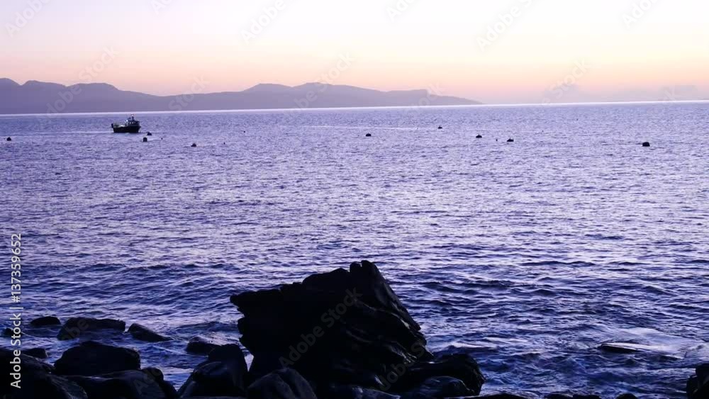 Minute before sunset. Anchored small fishing boat is swinging on sea ...