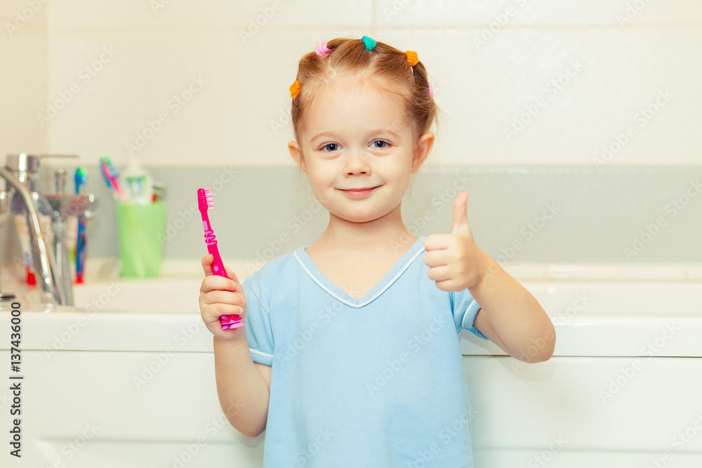 Little girl brushing her teeth in the bathroom. Smiling child holding ...