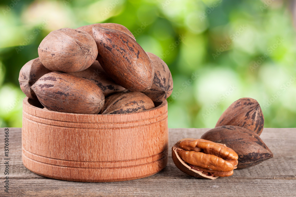 pecan nuts in a wooden bowl on the old board with blurred garden ...