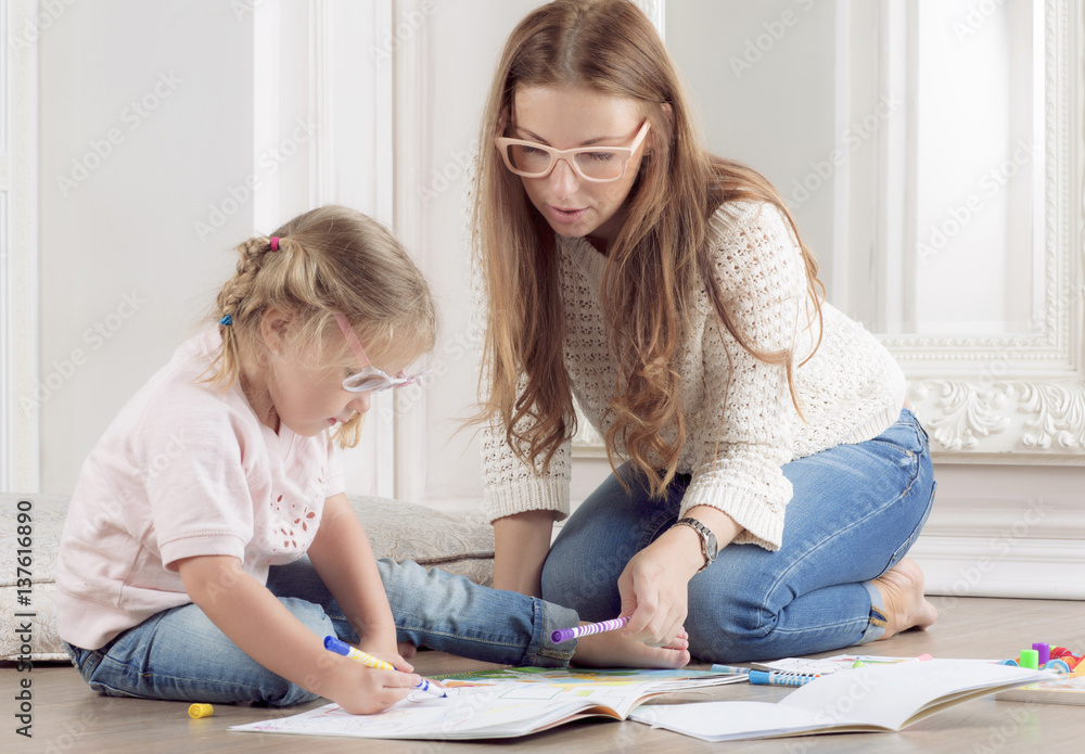 The daughter and mother sit on the floor and draw. The woman helps to ...