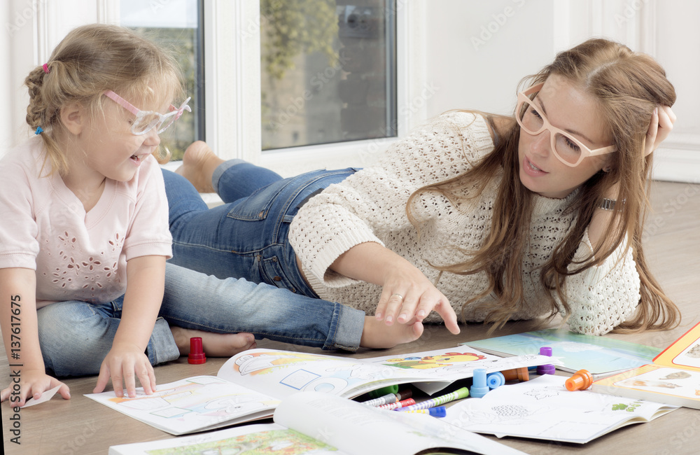 The daughter and mother sit on the floor and draw. The woman helps to ...