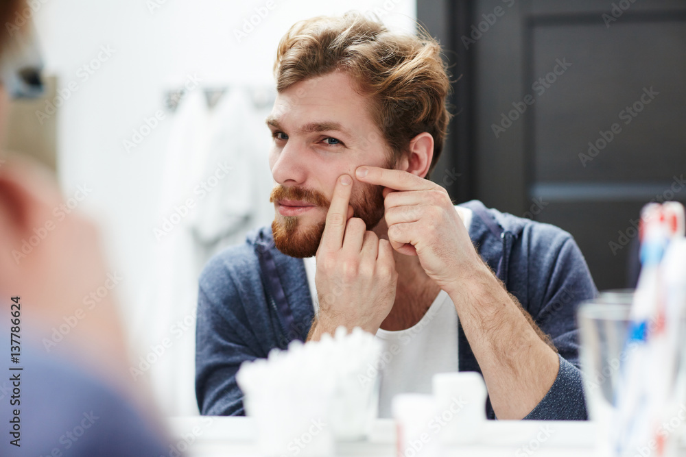 Young man squeezing pimple on his cheek in front of mirror Stock Photo ...