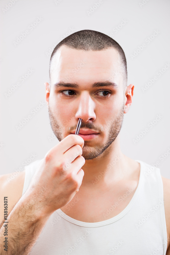 Young man is plucking nose hair with tweezers. Stock-Foto | Adobe Stock