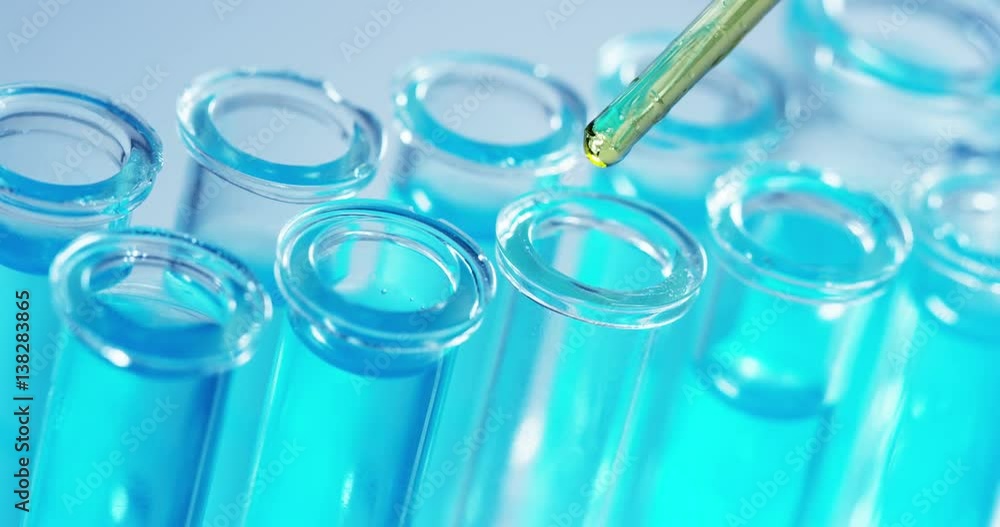 In a laboratory, a scientist with a pipette analyzes a colored liquid ...