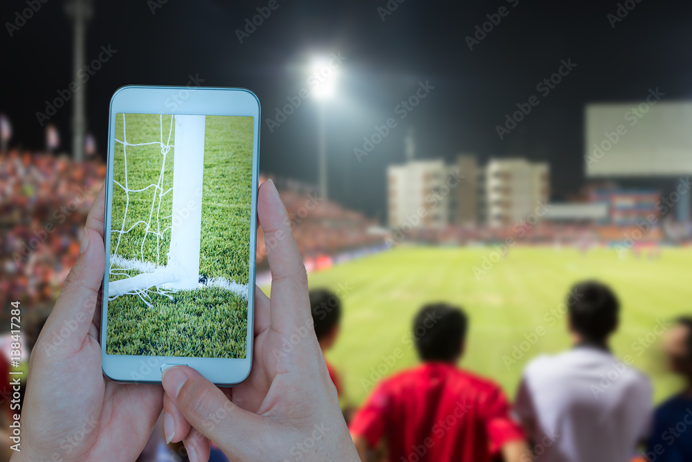 Hand holding smartphone with soccer screen in football stadium ...
