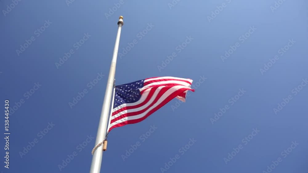 American flag flying at half mast aka half staff against a clear blue ...