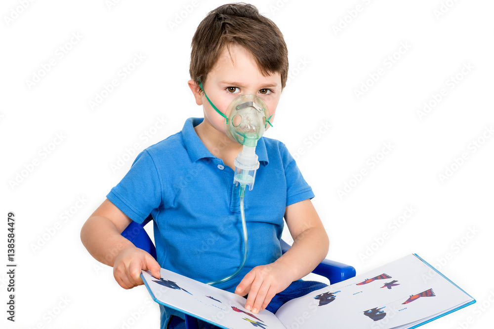 Asthmatic boy wearing face mask from nebulizer inhaler machine reading ...