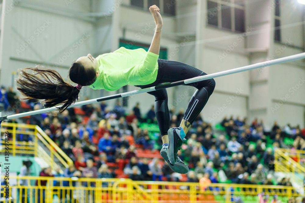 Young professional sportswoman jumping over bar in high jump ...
