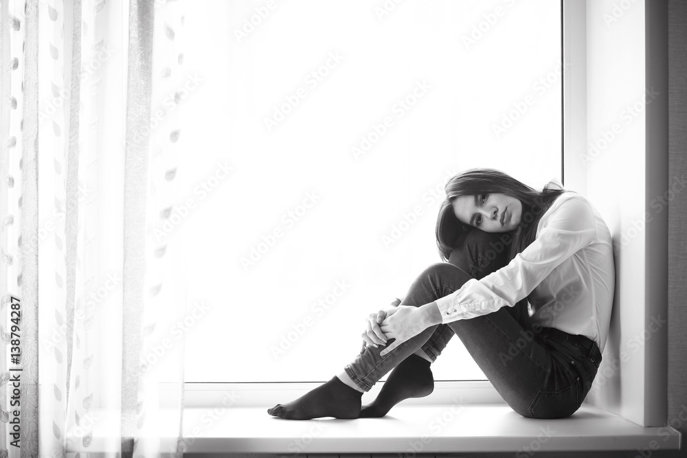 sad young adult woman sitting on a window Stock Photo | Adobe Stock