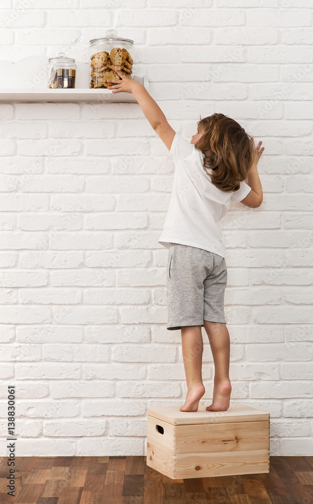 Cute little boy reaching for the cookies on the kitchen shelf Stock 写真 ...