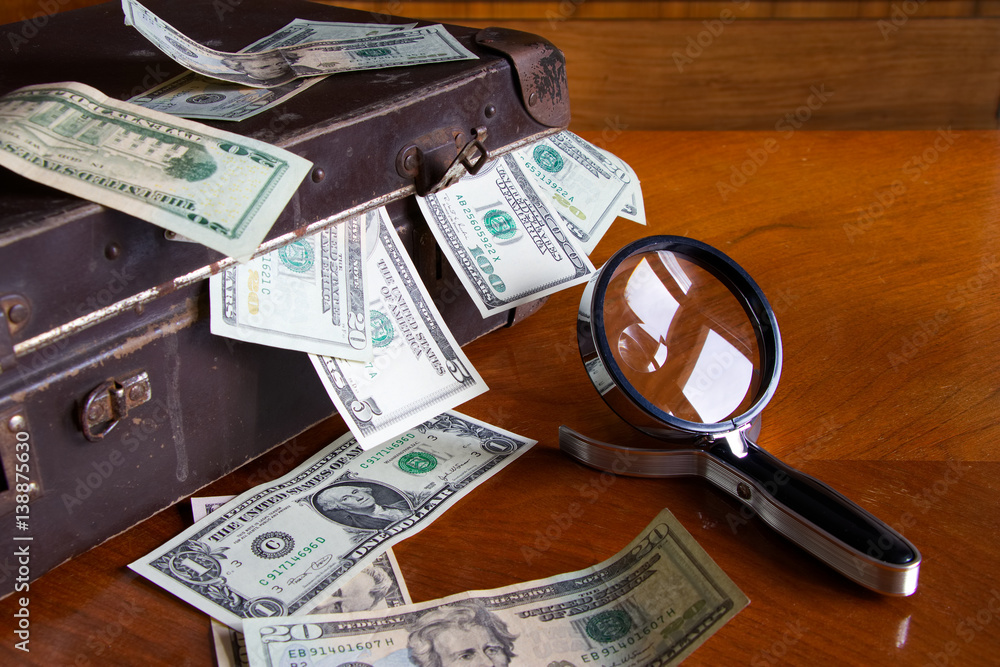 suitcase full of money on the table, magnifying glass as a symbol of ...