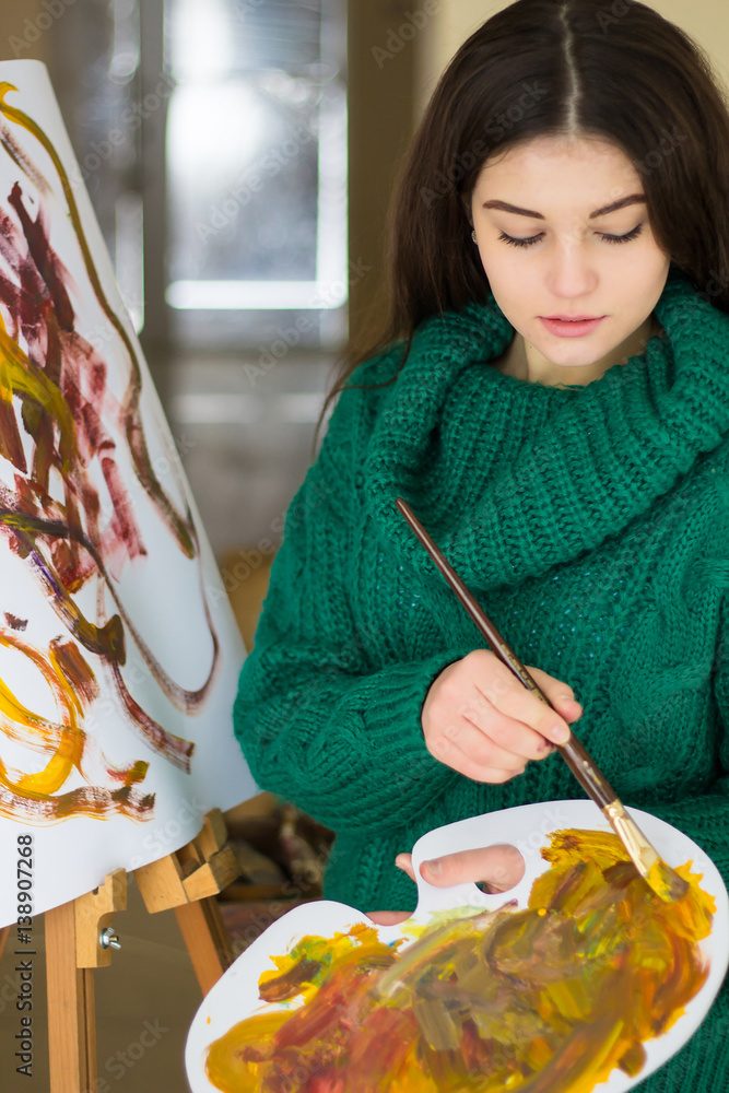 girl artist paints on canvas a painting on an easel. Model in the ...