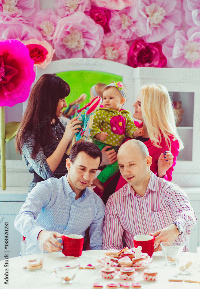 Two men drink tea at dinner table while two ladies play with little ...