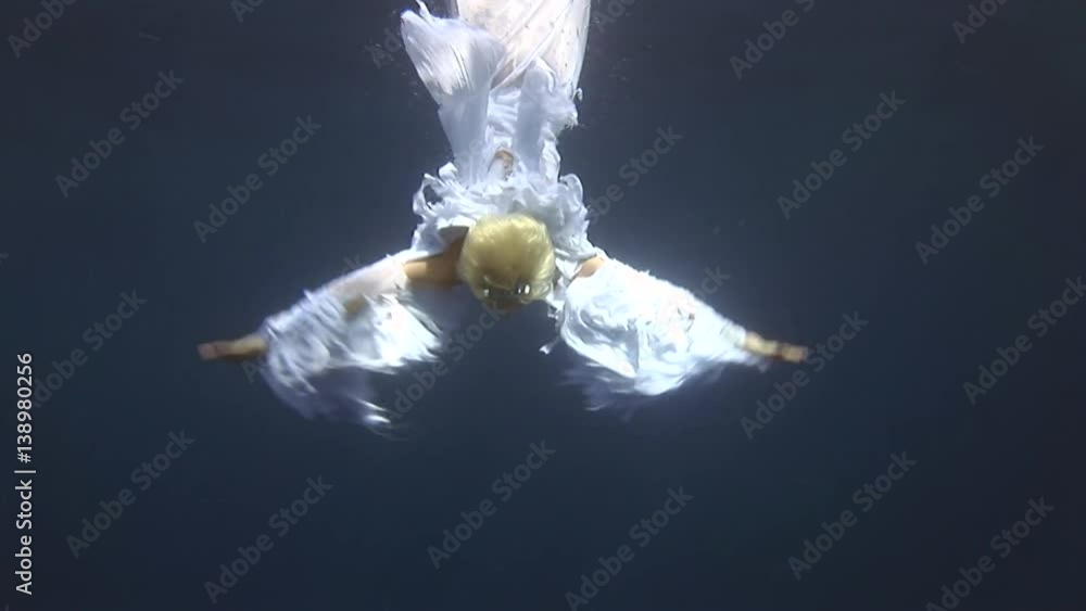 Underwater model free diver in costume angel swims in clean water in ...