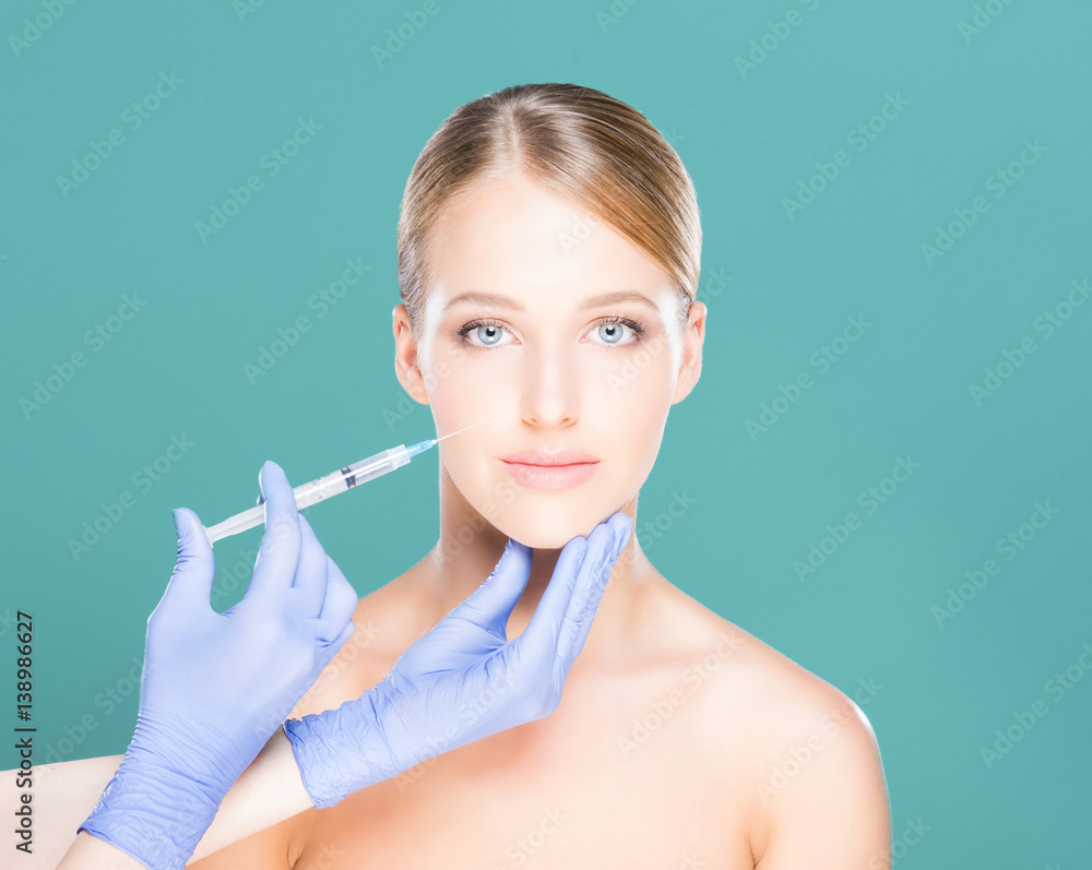 Young and beautiful woman having skin injections over teal background ...