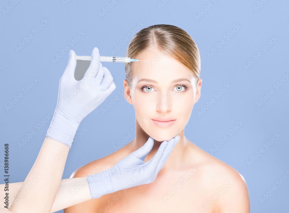 Young and beautiful woman having skin injections over blue background ...
