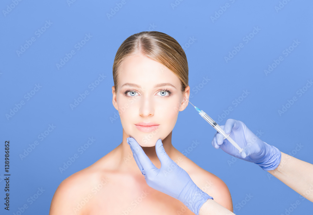 Doctor making injections in a beautiful face of a young woman over blue ...