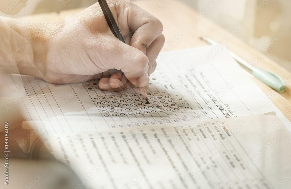Students hand holding pencil doing examination with blurred abstract ...