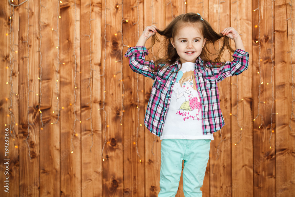 Little girl holds her dark blonde hait posing before wooden wall with ...
