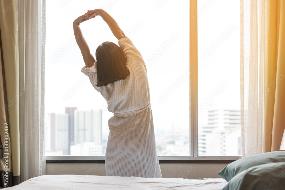 Happy healthy woman back view waking up stretching in bed room hotel ...