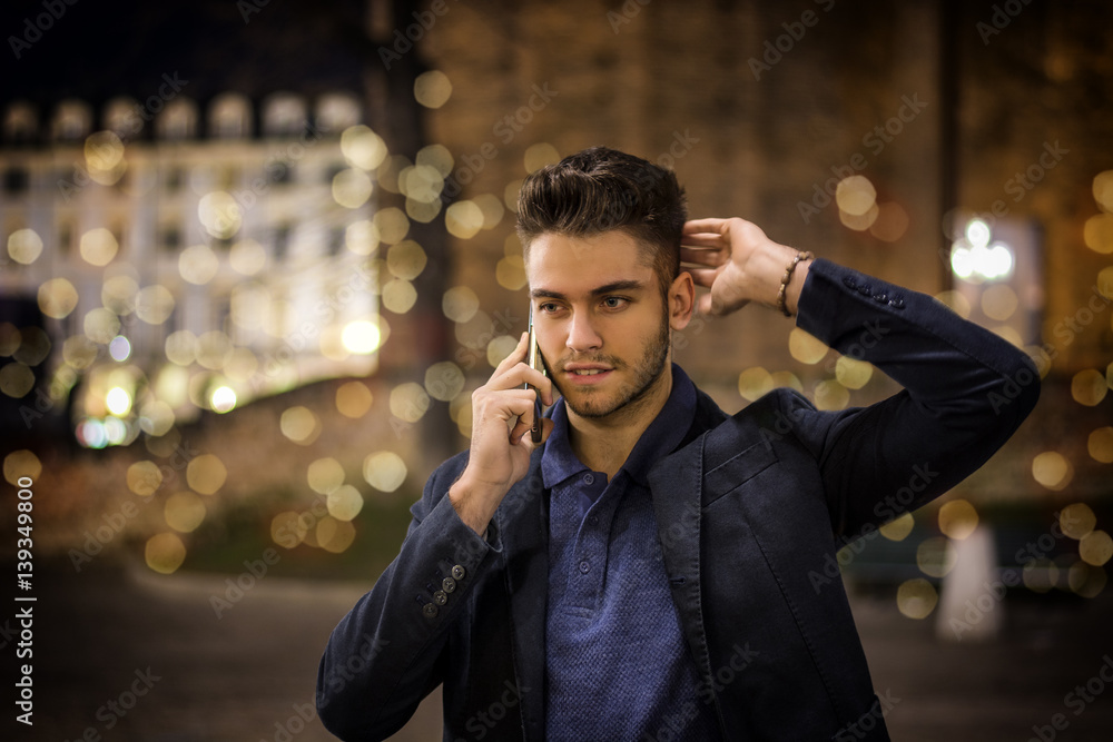Attractive young man portrait at night talking on the phone, with city ...