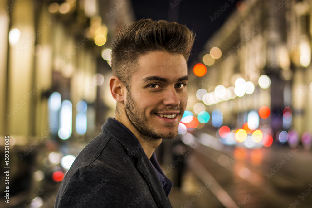 Attractive young man portrait at night with city lights behind him ...
