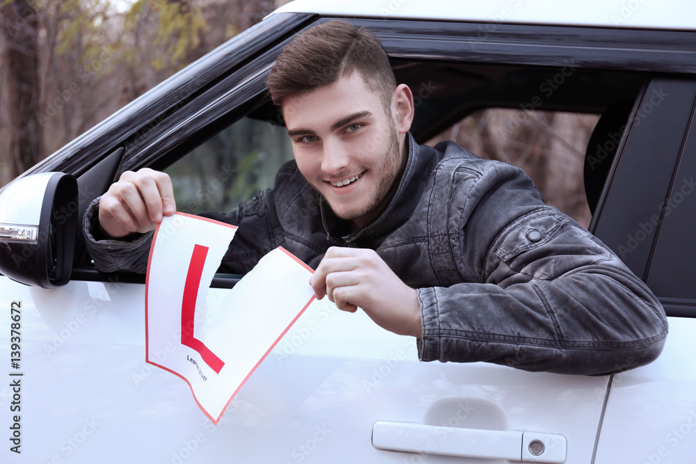 Young man tearing learner driver sign while looking out of car window ...