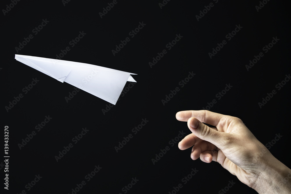 Image of a hand is throwing white paper plane on black background ...