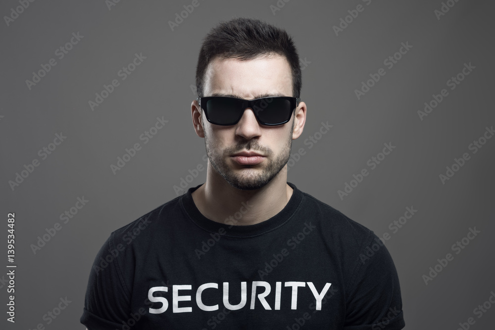Serious moody portrait of security guard wearing sunglasses looking at ...