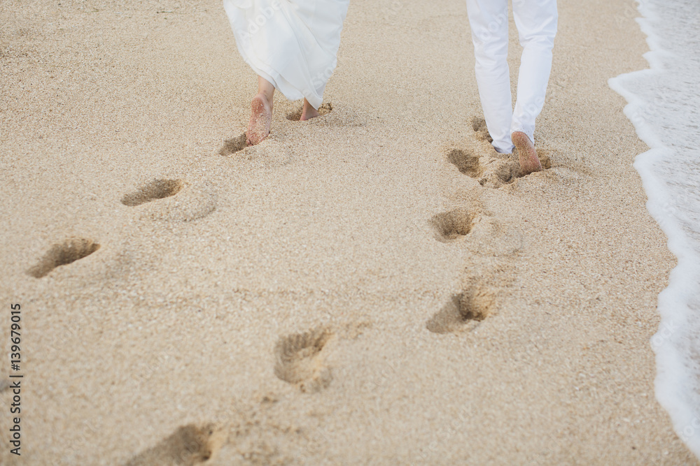 The bride and groom walk hand in the sand. footprints in the sand near ...