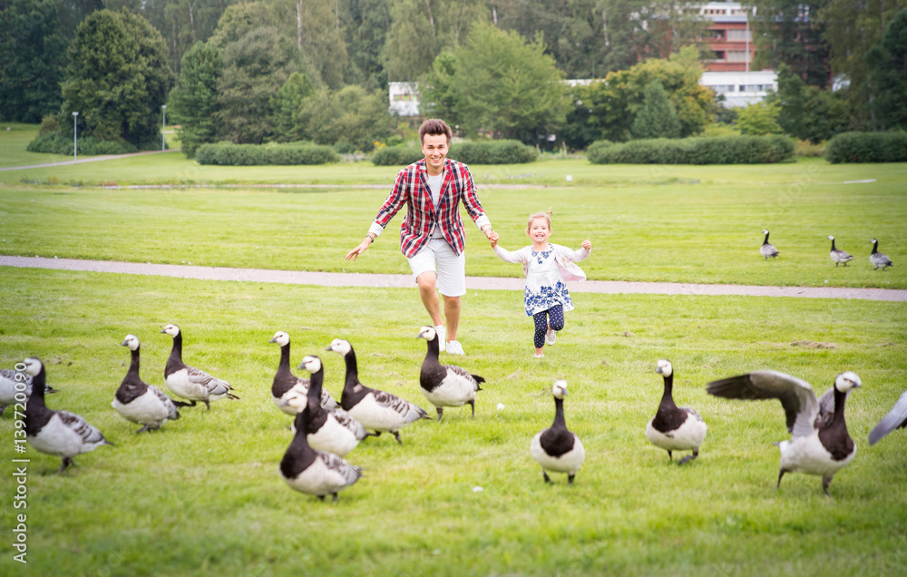 Father and daughter having fun in summer day. Chasing Canadian geese ...