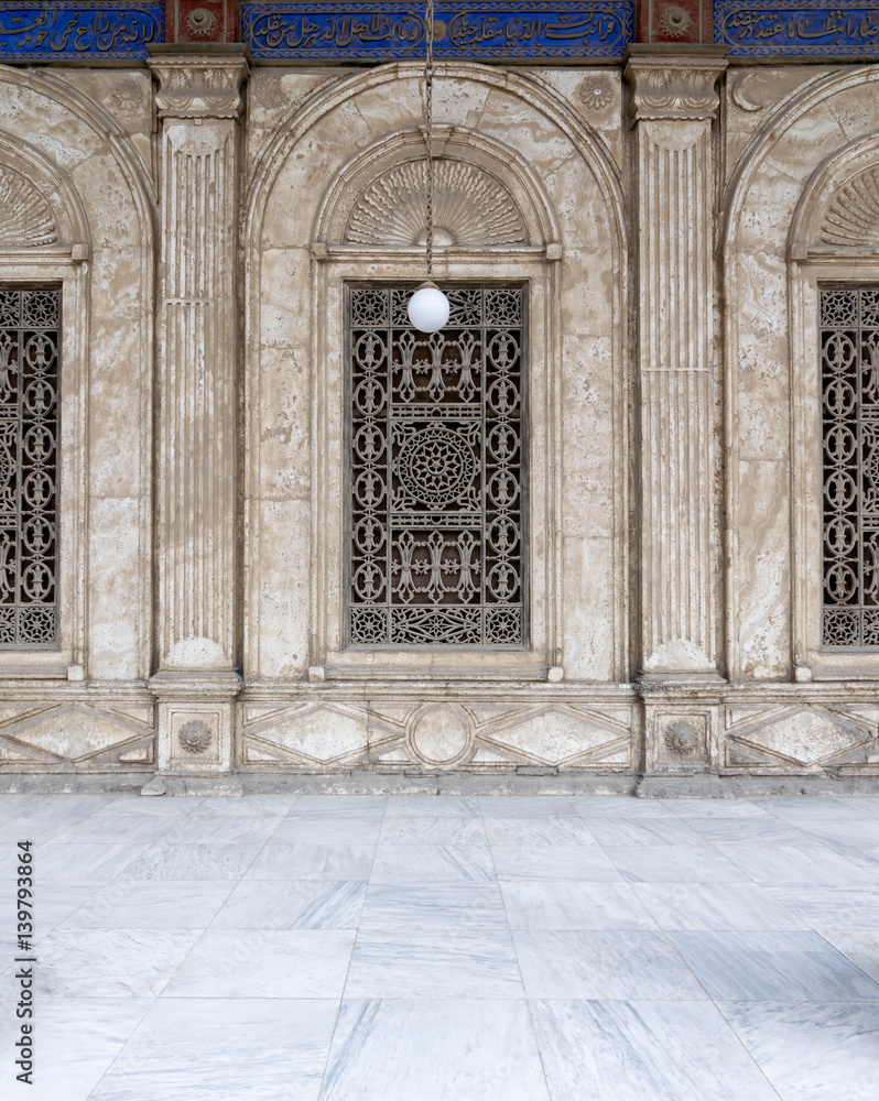 Three adjacent arched windows with decorated iron grid over white ...
