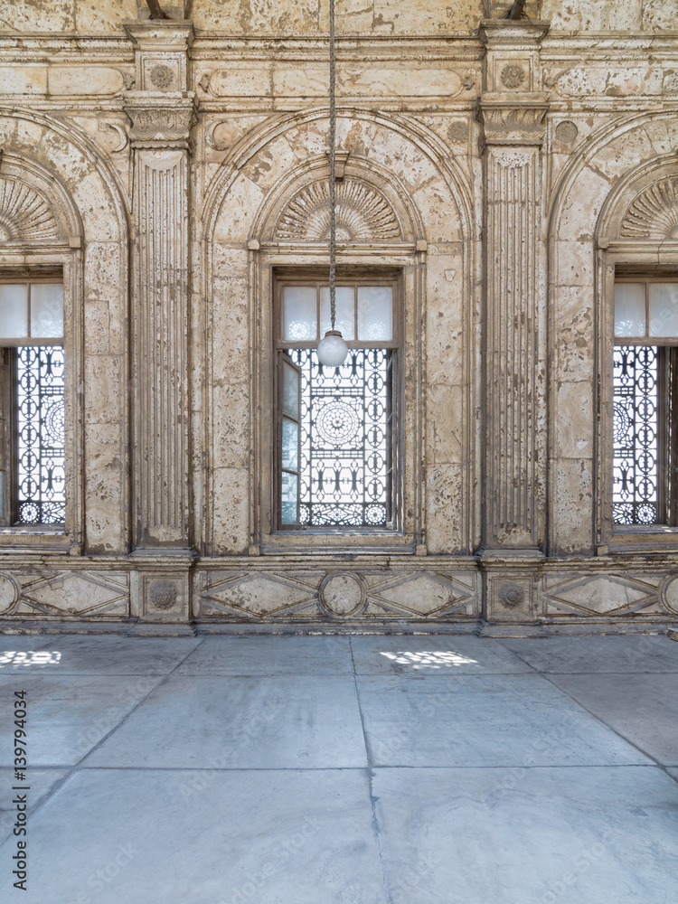 Three adjacent arched windows with decorated iron grid over white ...