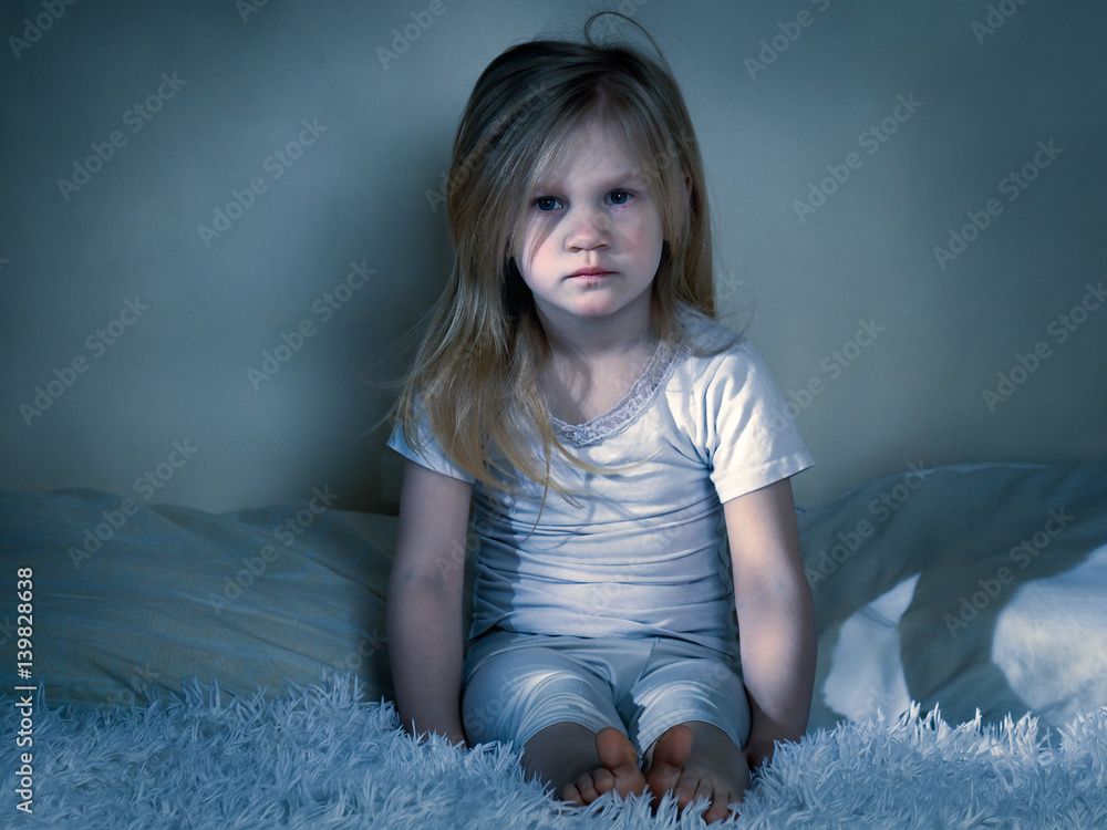 At night, the child is sitting on the bed. The girl scared. The concept ...
