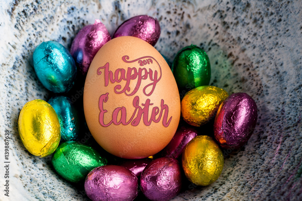 Happy Easter 2017 lettering on egg lined with small chocolate eggs wrapped in colorful foil ...