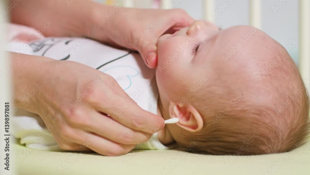 Mother is cleaning her baby ears close-up a small child lying on his ...