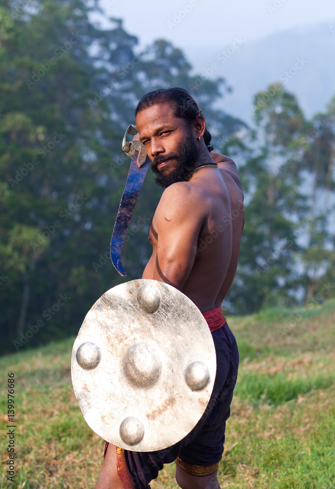 Indian fighter with sword and shield performing Kalaripayattu marital ...