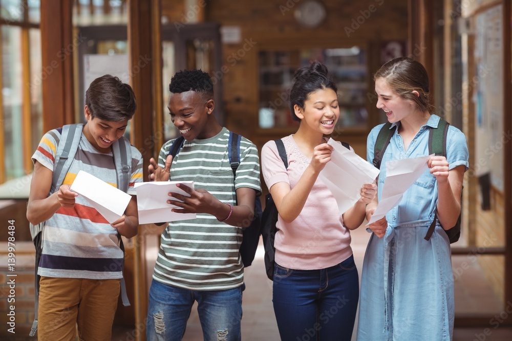 Happy classmates looking at grade cards in corridor Stock Photo | Adobe ...