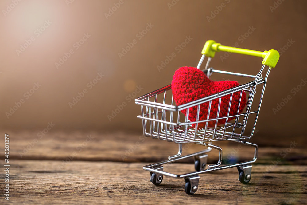 red heart shape in mini shopping cart on wooden mock up background ...
