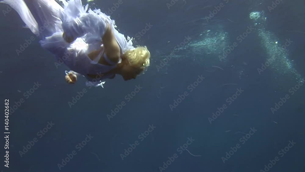 Underwater model free diver in costume angel swims in clean water in ...
