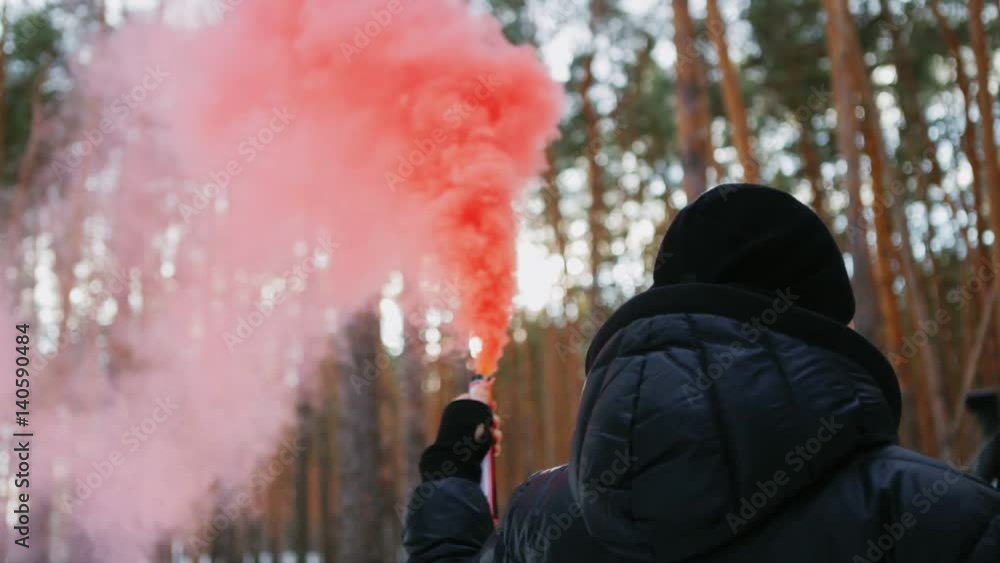 Red smoke erupts in the pine forest. The man in black clothes in the ...